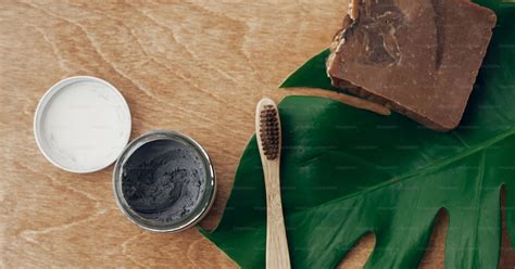 천연 치약 활성탄과 대나무 칫솔은 녹색 몬스테라 잎이 있는 나무 배경에 있습니다 플라스틱 프리 미용 필수품 치아 관리 폐기물 제로 개념 지속 가능한 라이프 스타일
