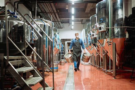 작업복과 보호 마스크를 쓴 현대 양조장의 젊은 남성 노동자가 거대한 강철 탱크의 줄을 따라 이동하면서 두 개의 수조를 들고 있습니다 사진 Unsplash의 공장 이미지