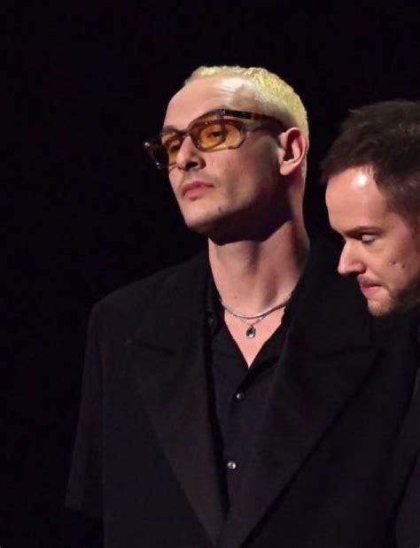 Two Men Standing Next To Each Other In Front Of A Dark Background With