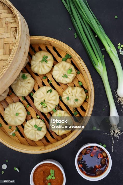 찐 모모 돼지 고기와 혼합 야채로 가득 찬 흰 밀가루 물 반죽 부추로 장식 칠리 오일 디핑 소스의 라메킨 옆에 뚜껑 대나무 증기선 검은 배경 높은 전망 0명에 대한 스톡