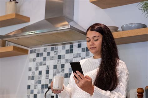 차 한 잔과 함께 부엌에 서있는 휴대 전화를 사용하는 여성 25 29세에 대한 스톡 사진 및 기타 이미지 25 29세 30 34세 Brand Name Smart