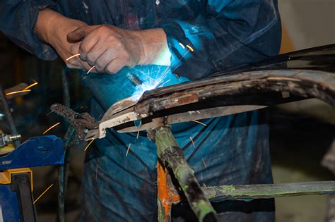 클로즈업 보기 강한 남자는 팔에 장갑 없이 작업 바지에 용접기입니다 금속 제품은 차고 워크샵에서 용접 기계로 용접 블루 연기와