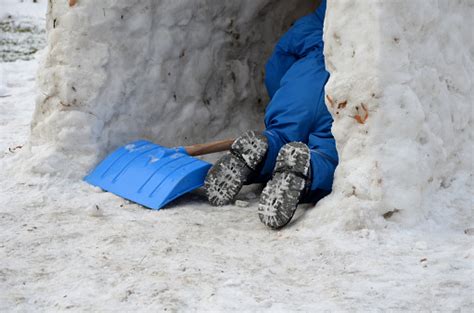 겨울 점프수트를 입은 어린 아이가 눈 위에 푸른 플라스틱 삽을 들고 걷고 있다 이글루를 만들 것입니다 어린 소년은 얼음 동굴 구멍 집으로 올라갑니다 그는 장갑과 나무