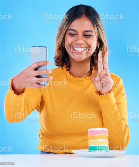 여자 케이크 평화 셀카는 스튜디오에서 미소를 짓고 먹게 되어 기쁩니다 행복한 여성과 손 이모티콘은 생일 축하를 위한 무지개 색 디저트와 함께 파란색 배경에 있다 생일에 대한