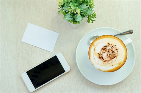 화이트 빈 비즈니스 카드와 스마트 흰색 컵에 라 떼 아트 커피와 함께 전화 나무 테이블에 공장을 조롱 복사 하 여 텍스트 또는