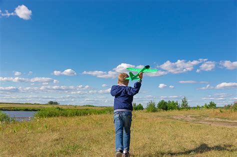 파란색 재킷을 입은 여섯 살 짜리 미취학 아동 소년이 여름날 구름이 있는 푸른 하늘을 배경으로 들판에서 장난감 비행기를
