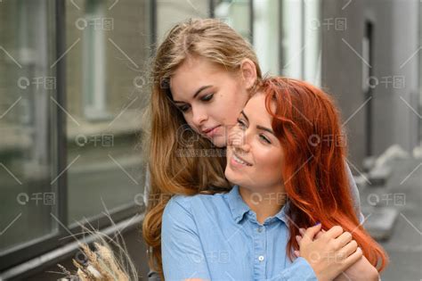 夫妇高清图片 同性关系。快乐的干花女同性恋夫妇。女孩从后面轻轻地拥抱着红发女友。靠近一双手。同性恋、双性恋或跨性别族群 同性关系。快乐的干花女