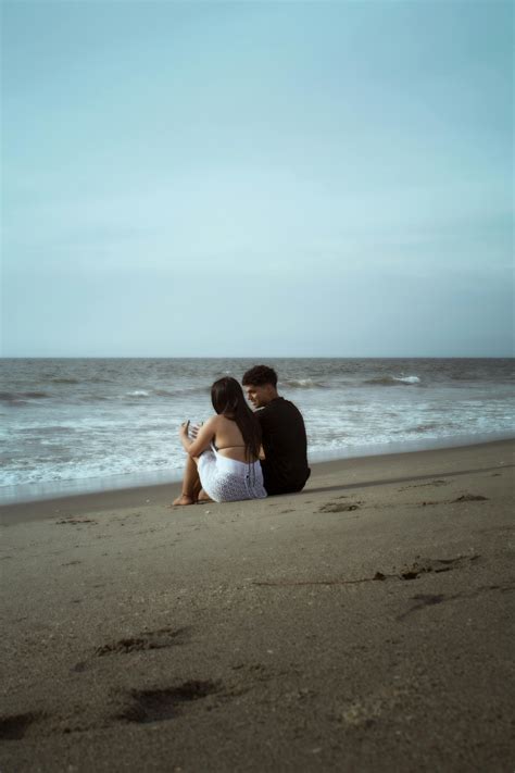 일몰 무렵 모래사장에 앉아 있는 로맨틱한 커플 · 무료 스톡 사진