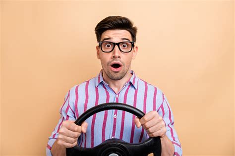 베이지 색 배경에 고립 된 예기치 않은 첫 번째 자동차 사고를 들고 스티어링 휠을 들고 젊은 충격 재미 있는 응시 남자의 사진 30 34세에 대한 스톡 사진 및 기타 이미지