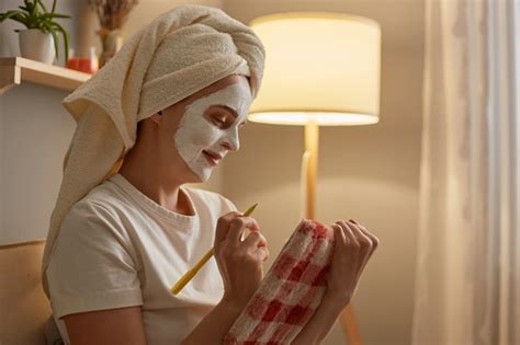 흰색 티셔츠를 입고 수건을 두르고 램프 근처에서 기침을 하고 주최자에 글을 쓰고 할 일 목록을 만들고 긍정적인 감정을 표현하는 만족스러운 여성의 프로필 초상화 쓰기에 대한