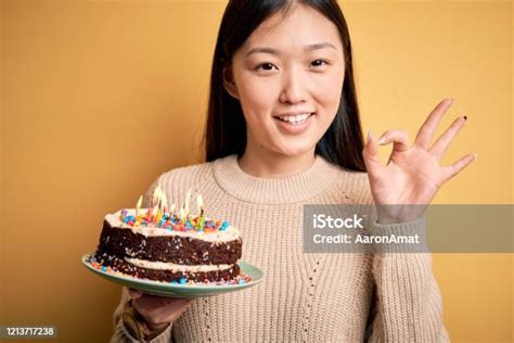 노란 고립 된 배경에 불타는 촛불로 생일 케이크를 들고 있는 젊은 아시아 여성은 손가락으로 확인 기호를하고 우수한 기호 개념에 대한 스톡 사진 및 기타 이미지 Istock