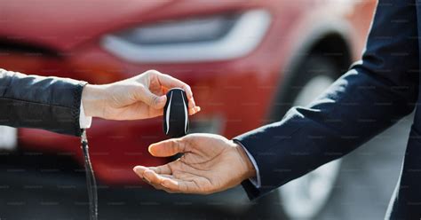 남성 고객에게 빨간색 전기 자동차에서 열쇠를 제시하는 여성 판매자의 클로즈업 고급 자동차의 배경을 흐리게합니다 성공적인 거래의 개념입니다 사진 Unsplash의