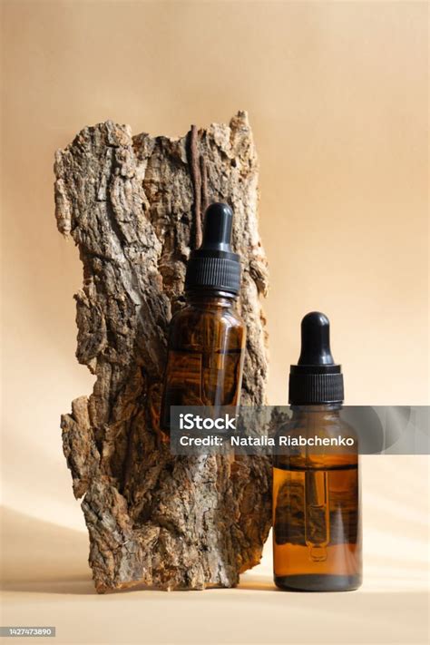 나무 껍질로 만든 스탠드에 점적기 뚜껑이있는 호박색 유리 병 두 개의 모형 햇빛 아래 베이지 색 배경에 콜라겐 보습 히알루 론산 세럼이있는 뚜렷하지 않은 용기 스포이드에