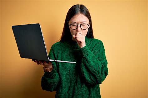 안경을 쓰고 컴퓨터 노트북을 사용하여 일하는 젊은 아시아 비즈니스 여성은 감기 또는 기관지염의 증상으로 기분이 나고 기침합니다