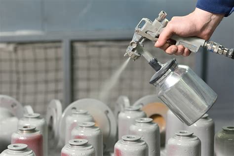 특별 한 방에서 공장에서 노동자는 스프레이 건에서 밸브의 부분을 페인트 회색 색깔 손 및 살포 총 가까이에 있는 페인트 벨 브