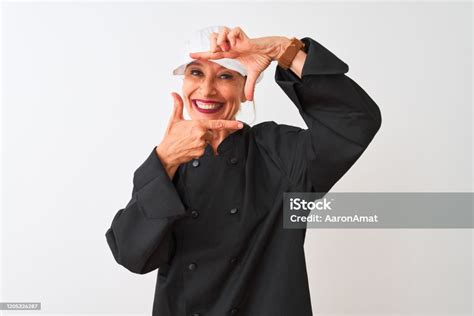 유니폼과 모자를 입고 고립 된 흰색 배경 위에 서있는 중년 요리사 여성은 행복한 얼굴로 손과 손가락으로 프레임을 만드는 미소