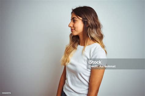 캐주얼 한 흰색 티셔츠를 입고 옆으로 찾고 고립 된 배경위에 젊은 아름다운 여성 자연스러운 얼굴과 자신감 있는 미소로 프로필 포즈를 취합니다 T 셔츠에 대한 스톡 사진 및