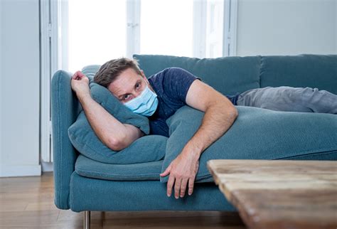 코로나바이러스 사망 직장 분실 잠금 및 사회적 불변으로 인해 피곤하고 걱정스러운 고통을 느끼는 집 거실 소파에서 보호 얼굴 마스크를 쓴 슬픈 남자 정신 건강과 격리 개념