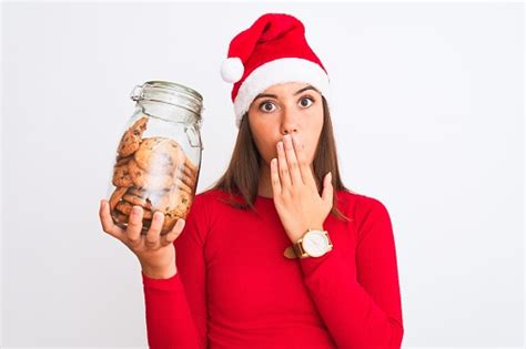 실수 두려움의 표정 침묵 비밀 개념에 무서워 손으로 고립 된 흰색 배경 커버 입에 쿠키의 항아리를 들고 크리스마스 산타 모자를 입고 아름다운 소녀 12월에 대한 스톡 사진