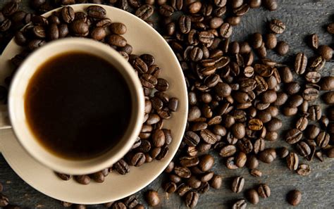 나무 테이블 배경에 구운 커피 콩커피 컵 나무 테이블에 흩어져 있는 커피 콩이 있는 검은 색 코프 잔 신선한 커피 콩 갈색에 대한 스톡 사진 및 기타 이미지 Istock