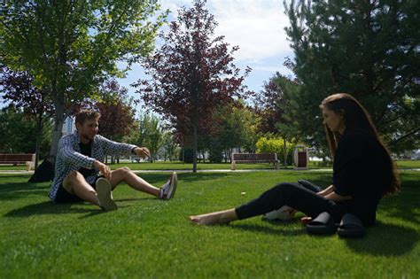 한 남자와 한 여자가 공원의 푸른 잔디밭에 앉아 가벼운 대화를 나누고 있습니다 그들은 나무와 자연에 둘러싸인 아름다운 화창한