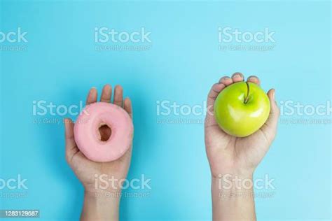 녹색 사과와 분홍색 도넛을 들고 있는 여성 과일 중에서 선택하는 여성은 건강한 음식이며 달콤한 것은 건강에 해로운 정크