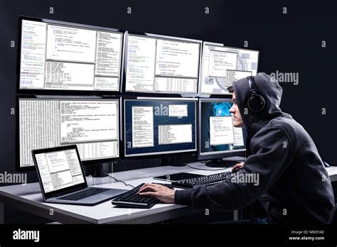 Rear View Of A Hacker Using Multiple Computers For Stealing Data In