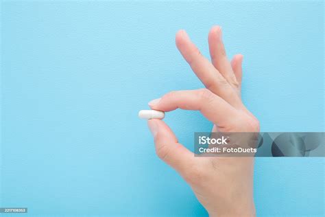 젊은 성인 여자 손 손가락 들고 하늘색 배경에 흰색 캡슐 알약 근접 촬영 파스텔 색상 비타민이나 약을 받고 있습니다 정면 View 건강관리와 의술에 대한 스톡 사진 및 기타