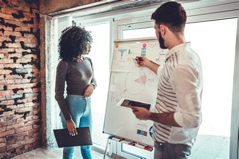 사업가와 사업가가 손에 마커가 있는 화이트보드 근처에 서서 태블릿 화면을 바라보고 있습니다 비즈니스에 대한 스톡 사진 및 기타 이미지 Istock