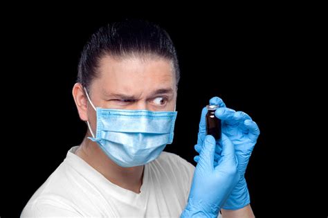 의료 용 마스크의 의사가 질병 치료를위한 백신이있는 유리 병을 멸균 장갑에 손에 쥐고있는 재미있는 남성 초상화는 검은 배경에