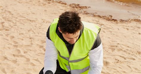 제복을 입은 젊은 현대 자원봉사자가 모래사장에서 일하는 동안 쓰레기를 줍고 있다 사진 Unsplash의 청소 이미지