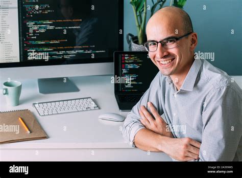 Programmer Working Behind The Desk With Two Screens Filled With Code