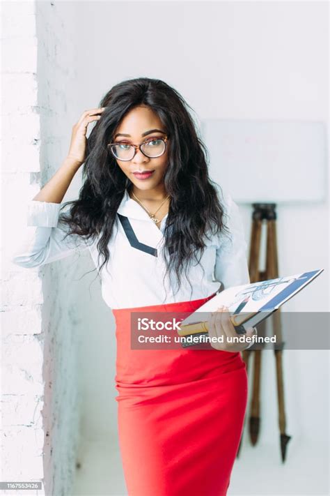 큰 창문 근처의 흰색 배경에 서있는 책과 문서를 들고 안경을 쓴 아프리카계 미국인 비즈니스 여성 또는 교사 40 49세에 대한 스톡 사진 및 기타 이미지 Istock