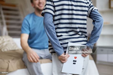 아버지의 날과 함께 그를 축하하는 동안 뒤에 뒤에 아버지를위한 카드를 숨기고 벗겨진 티셔츠에 인식 할 수없는 아이의 클로즈업