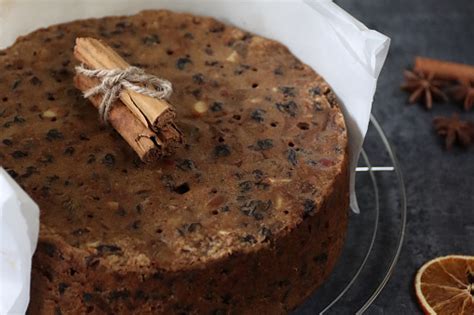 홈메이드의 클로즈업 이미지 냉각 랙에 계피 스틱 번들 얹은 크리스마스 과일 케이크 기름진 양피지 종이 말린 감귤류 오렌지 과일 조각 스타 아니스 회색 배경 높은 전망 전경에