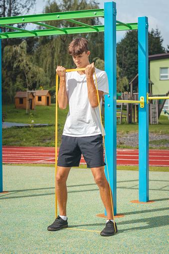 저항 고무를 사용하여 몸을 단련하는 목표 지향적인 십대는 근력 운동을 수행합니다 스포츠 시즌을 준비합니다 자신의 몸으로 운동하기 야외 운동 놀이터 청소년기에 대한 스톡 사진