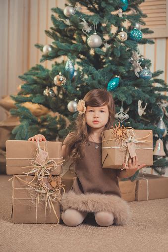 젊은 갈색 머리 인형 아가씨 아가씨 세련 된 모피 크리스마스 새 해 트리 가까운 스튜디오에 앉아 서 포즈와 아늑한 따뜻한 겨울 회색 재킷을 입고 하 고 선물 한다 구석에