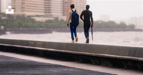 건물을 배경으로 물가의 콘크리트 산책로를 걷고 있는 남자와 여자 사진 Unsplash의 무료 여행하다 이미지