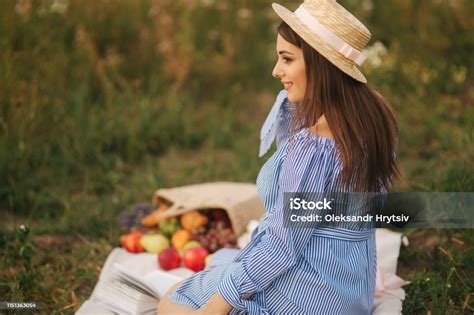 매력적인 임신한 여성은 격자 무늬에 앉아 있습니다 여자는 파란 드레스와 니트 모자를 입고 그녀는 과일 바구니를가지고 농장의 배경