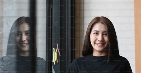 디지털 태블릿을 들고 사무실의 창문 근처에 서서 카메라를 향해 웃고 있는 젊은 사업가의 초상화 사진 Unsplash의 태국 이미지