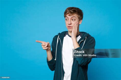 캐주얼에 당황 하는 혐오 젊은 남자는 뺨에 손을 퍼 팅 및 옆에 파란 벽 배경에 고립 된 검지 손가락 사람들은 진심으로 감정 라이프 스타일 개념입니다 복사 공간을 모의