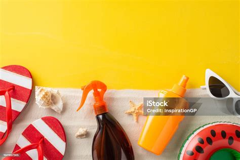 생생한 노란색과 모래를 배경으로 자외선 차단 오일과 Spf 로션 병 유리잔 고무 링 슬리퍼 조개껍데기 불가사리가 있는 해변 필수품 탑 뷰 배열 텍스트 또는 광고를 위한 빈