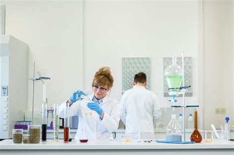 안경을 쓴 여성 화학 과학자는 실험실에서 대마 Cbd 및 Cbda 오일과 함께 작동합니다 그녀는 라텍스 장갑 유리 튜브 및 에렌마이어 플라스크를 사용하고 있습니다 대마초