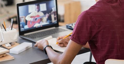 테이블 옆에 앉아 노트북 화면에 기타를 들고 음악 선생님을 보면서 메모를 하는 혼혈 남자 사진 Unsplash의 테이블 이미지