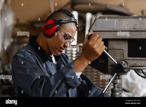 Side View Portrait Of Female Worker Operating Machine Units In Industrial Workshop And Wearing