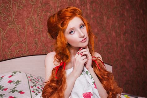 긴 붉은 곱슬 머리를 가진 여자는 담요 아래 침대에서 잠 옷에 머리 띠에 모였다 예쁜 얼굴 창백한 피부 파란 눈 및 침실에 밝은 특이 한 모양으로 빨간 머리 소녀 가정의