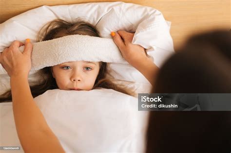 어머니의 클로즈업은 집에서 담요 아래에 누워 발열과 아픈 딸의 온도를 낮추기 위해 이마에 압축을 넣어 2명에 대한 스톡 사진 및