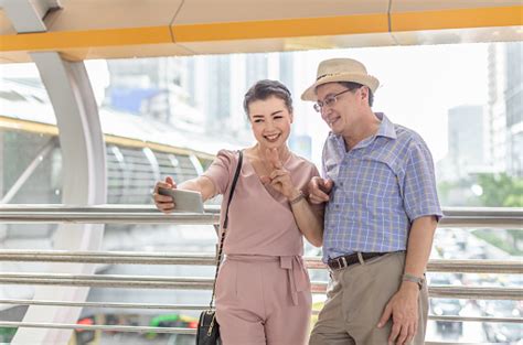 시니어 부부는 함께 여행하고 셀카를 찍고 가방과 모자를 들고 도시 흐림 배경을 배경으로 합니다 2명에 대한 스톡 사진 및 기타 이미지 Istock