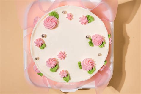 베이지색 배경에 흰색 선물 상자에 분홍색 크림 치즈 꽃으로 장식된 작은 한국 스타일의 트렌디한 도시락 케이크 사랑하는 사람을위한 선물로 케이크 여자를위한 봄 부드러운