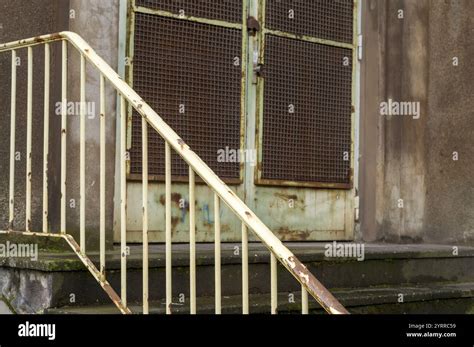 Rusty Metal Door With Mesh Screen And A Rusty Handrail Leading Up Steps To An Old Building